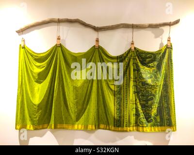 A silk saree suspended in four sections from a tree branch hanger makes ...