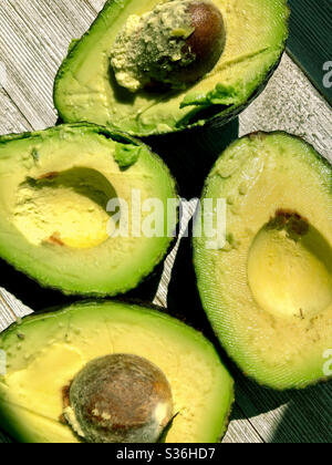 Avocado cut in half, seed and pulp visible, two more whole pears on ...