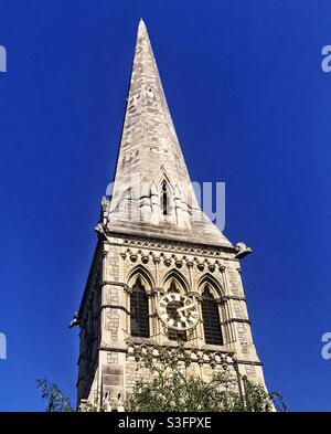 The broach spire of Holy Trinity Church above treetops lit by the ...