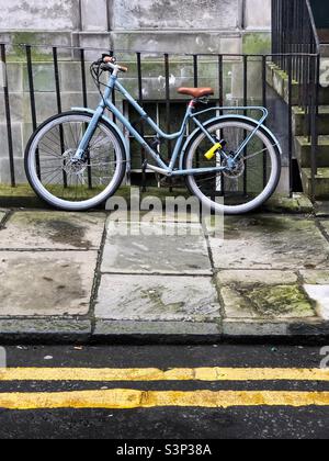 Old style bicycle bike chained to a drain pipe leaning against a red ...