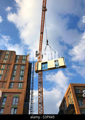 A prefabricated piece of a new building being lifted into place by a ...