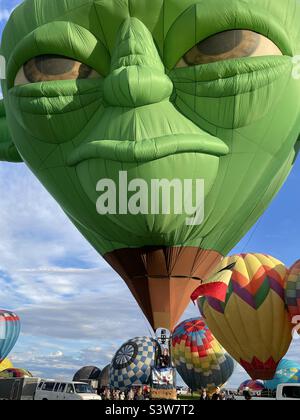A green hot air balloon with Alien face on it floating against a blue ...