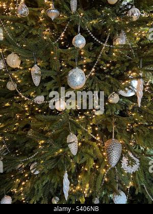 A white Christmas tree is decorated with silver plastic toys. Bright ...