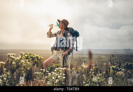 Tired female hiker taking a break and wiping sweat from her forehead ...