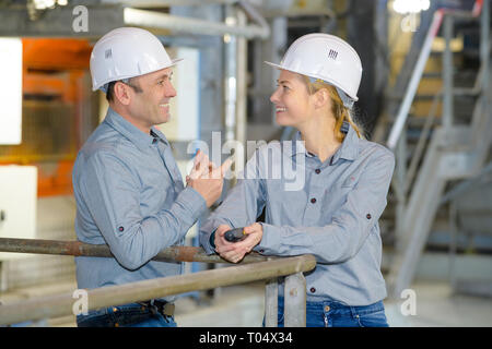 Pretty young woman controlling process in the factory with male worker ...