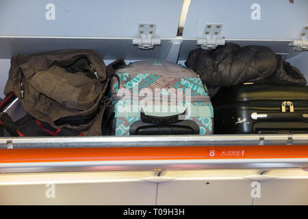 A plane passenger storing hand luggage in the overhead locker on a ...