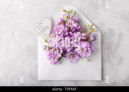 Lilac matthiola flowers in an envelope over light gray stone background ...