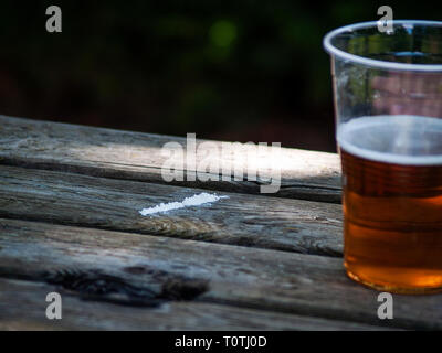 A line of cocaine on a wooden table with a glass of beer on the side ...