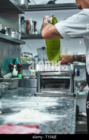 Cropped image of man rolling dough by basil plants at kitchen table ...