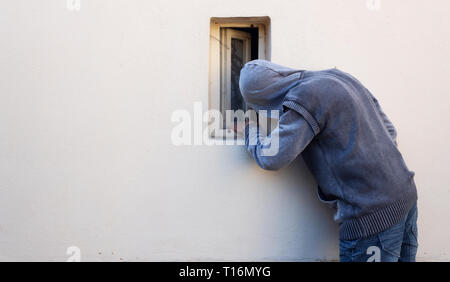 Man wearing hoodie at window looking at LCD screen of camera which has ...