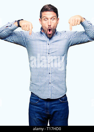 Handsome caucasian man pointing down with impressed and happy face ...