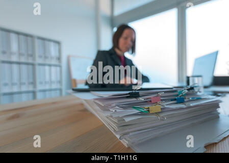 Busy businesswoman doing paperwork in office at the desk filled with ...