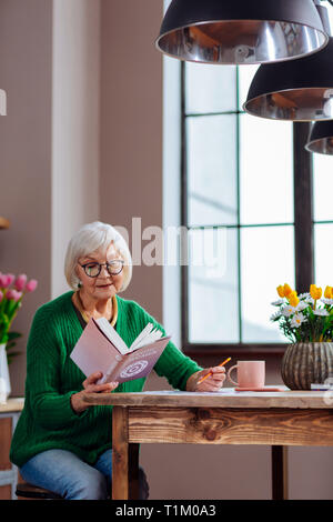 Charming woman writing down notes and drinking tea while working with ...