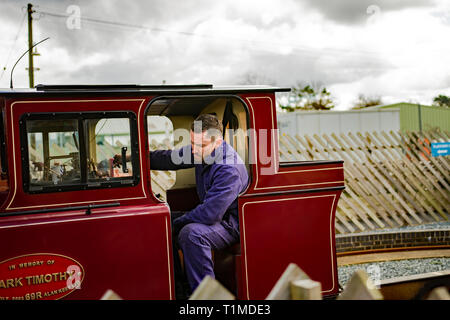A train engineer in blue overalls crouching down and applying motor oil ...