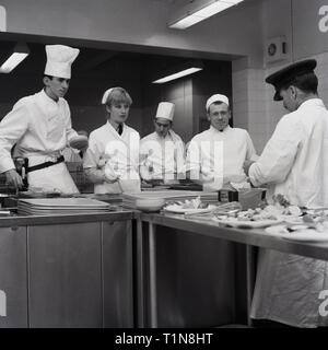 1967, white-coated trainee chefs under supervision preparing food in a ...