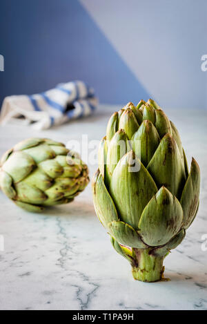 Two ripe artichokes with purple green hues rest on weathered ...