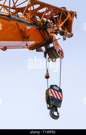 A orange crane boom with hooks on a blue sky background with clipping ...