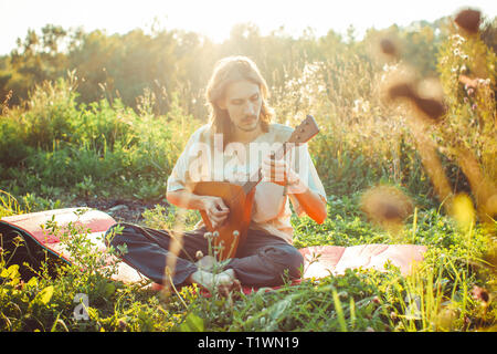 a man plays a balalaika sitting on the grass in the forest Stock Photo ...