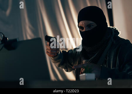 Aggressive criminal pointing with finger and aiming gun at laptop ...