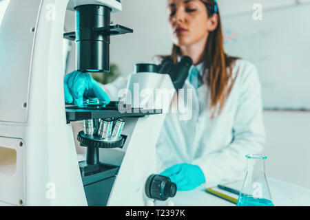 Scientist analyzing microscope slide at laboratory. Young woman ...