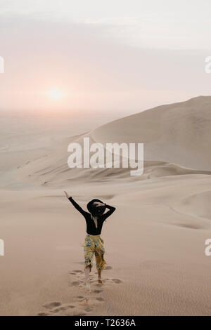Namibia, Namib, back view of woman walking barefoot on desert dune ...