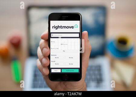 A man looks at his iPhone which displays the Rightmove logo, while sat ...