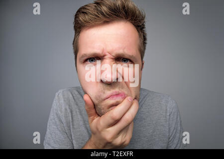 Puzzled young man keeps lips pressed, has frustrated facial expression ...