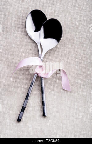Two spoons tied together with pink ribbon.On a white background ...