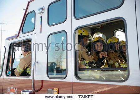 Image of a group of firefighters in uniform riding on the outside of an ...