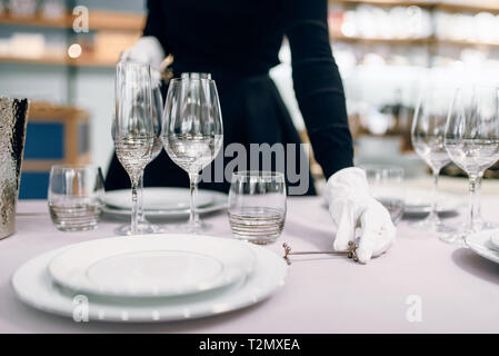 Waitress in gloves puts the dishes for dining, table setting. Serving ...
