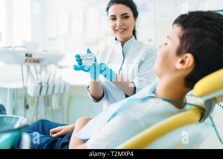 Female dentist shows dentures to little boy in a dental chair ...