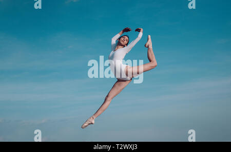 Feels like flying. Young ballerina jumping on blue sky. Pretty girl in ...