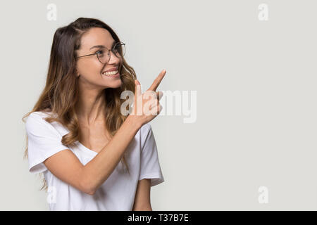 Cheerful woman in eyewear pointing finger left at logo, smiling happy ...