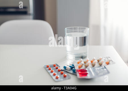Medicine and water on table with sick person blurred in background ...