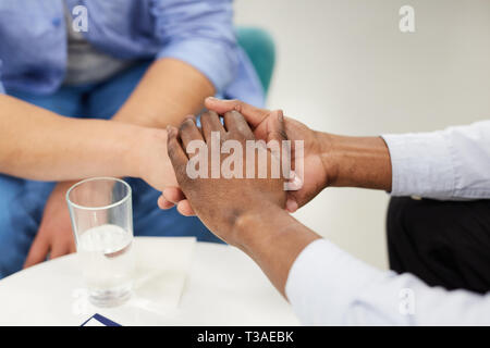 A close-up of a caring psychologist holding a patient's hand to comfort ...