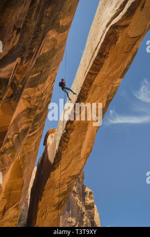 Rock climber dangling in mid air after rappelling past an overhang ...