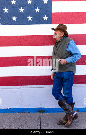 Old cowboy with gray beard stands next to a white and red wall Stock ...