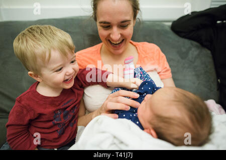 Happy mother smiles at baby sitting on bed in room. Motherhood. Mothers ...
