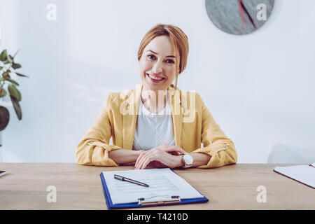 happy recruiter in yellow jacket sitting near clipboard and pen Stock ...