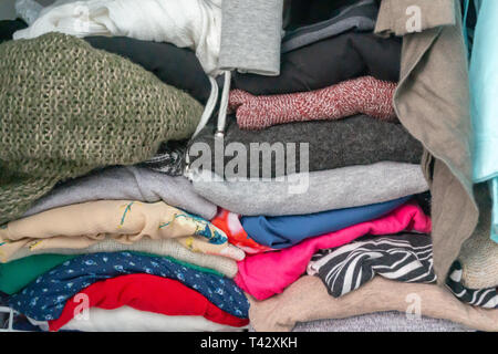 Messy folded clothes crammed in a closet on a shelf. Depicting woman's ...