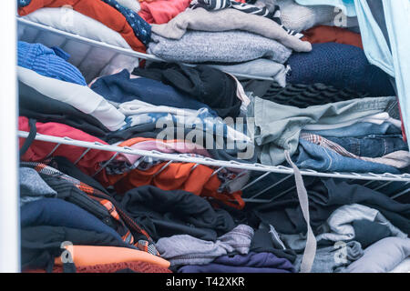 Messy folded clothes crammed in a closet on a shelf. Depicting woman's ...