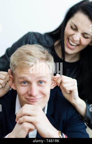 Girl pulling boyfriend's ears to make a fun. Blond man in formal dress ...
