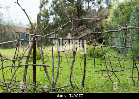 Rustic fence made with tree branches and wooden posts with a small roof ...