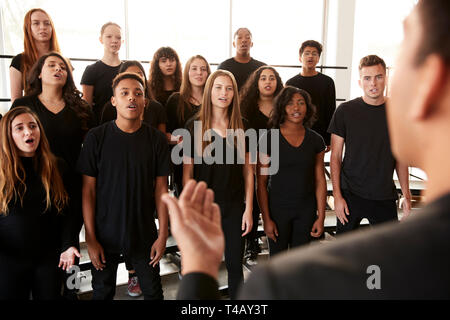 Female teacher singing choir with students holding sheet in classroom ...