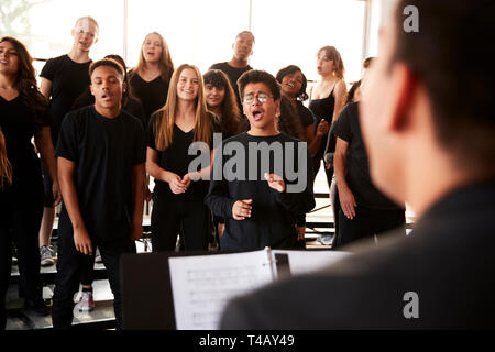 Female teacher singing choir with students holding sheet in classroom ...