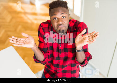 African American man at home clueless and confused expression with arms ...