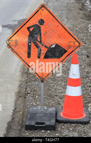 Orange pictogram Men at Work warning sign on metal pole against a blue ...