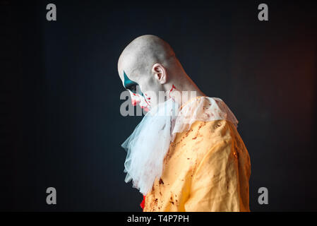 Sad bloody clown with makeup in carnival costume, side view. Crazy ...