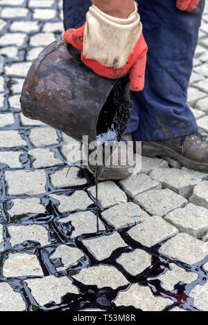 Worker pouring bitumen to apply the joint of road. Traditional pitch ...