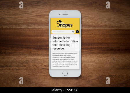 An iPhone showing the Snopes website rests on a yellow background table ...